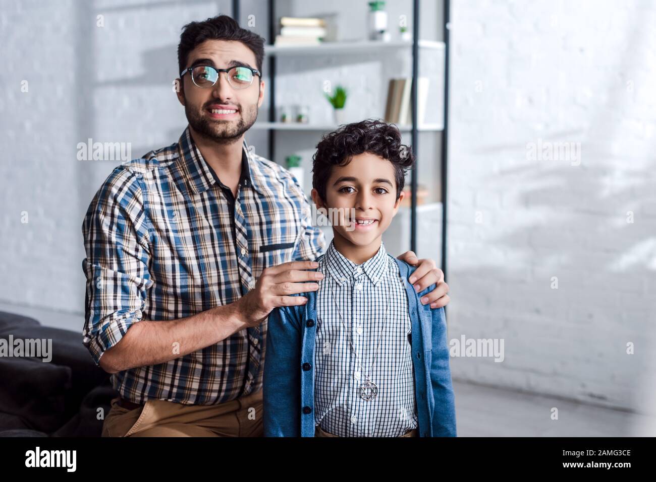 smiling jewish father hugging son and looking at camera in apartment ...