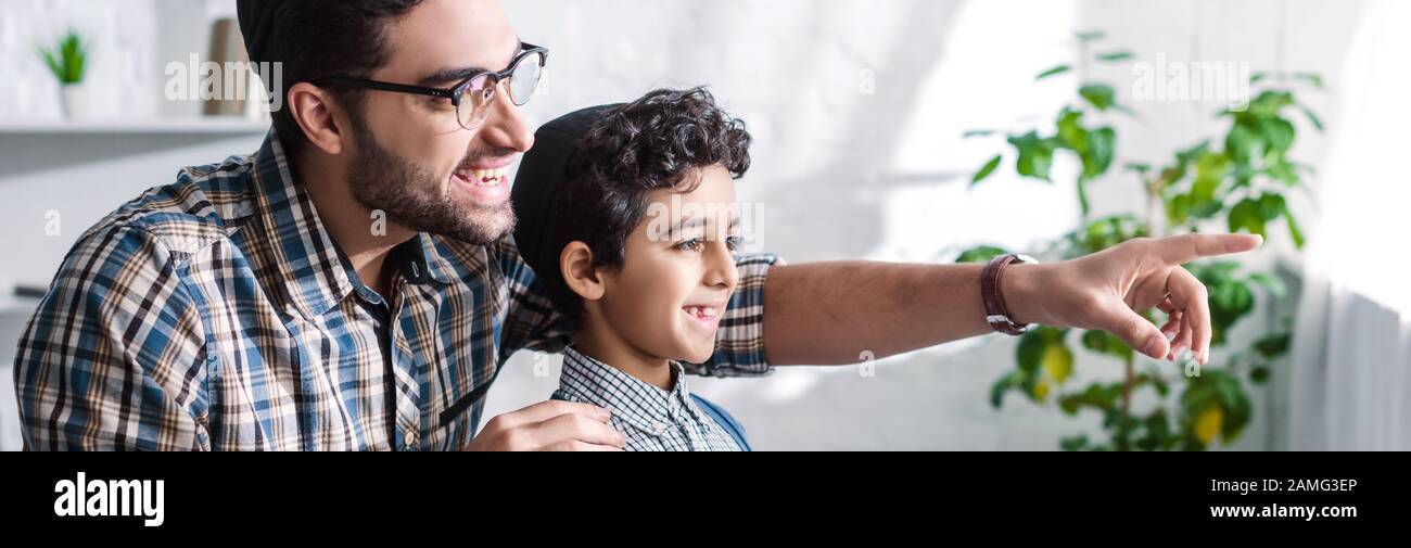 panoramic shot of smiling jewish father pointing with finger and ...
