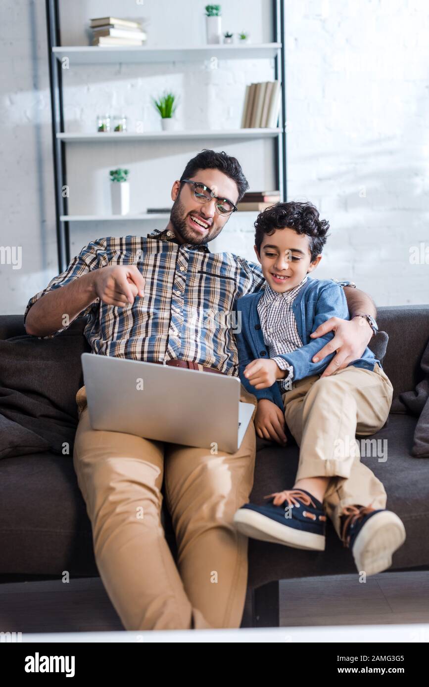 smiling jewish father pointing with finger at laptop and hugging son in ...