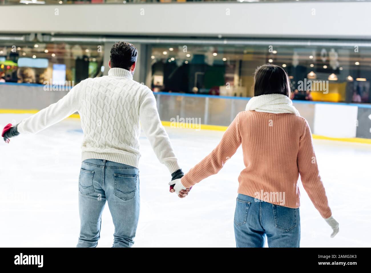 back view of young couple holding hands on skating rink Stock Photo - Alamy