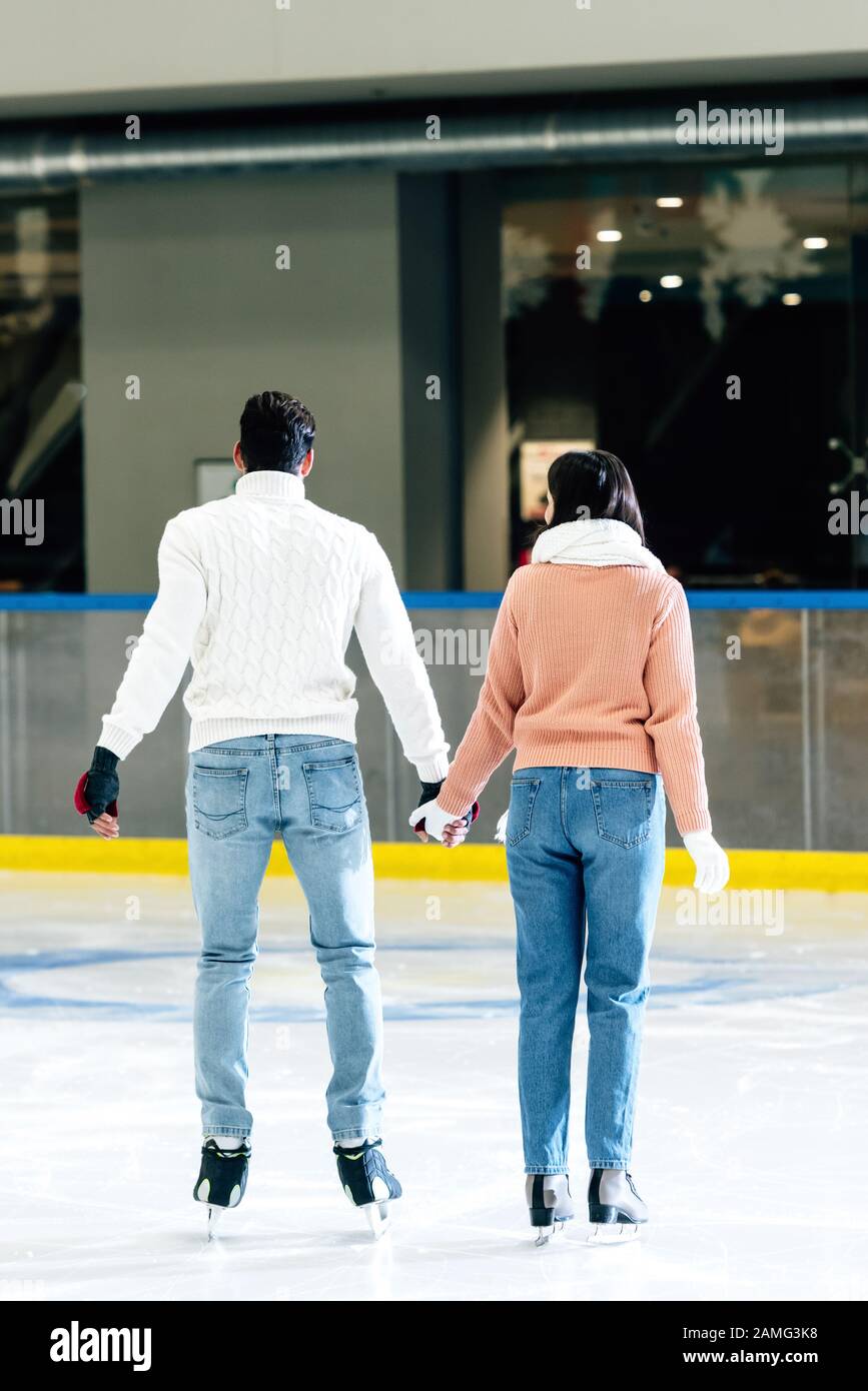 back view of young couple holding hands on skating rink Stock Photo - Alamy