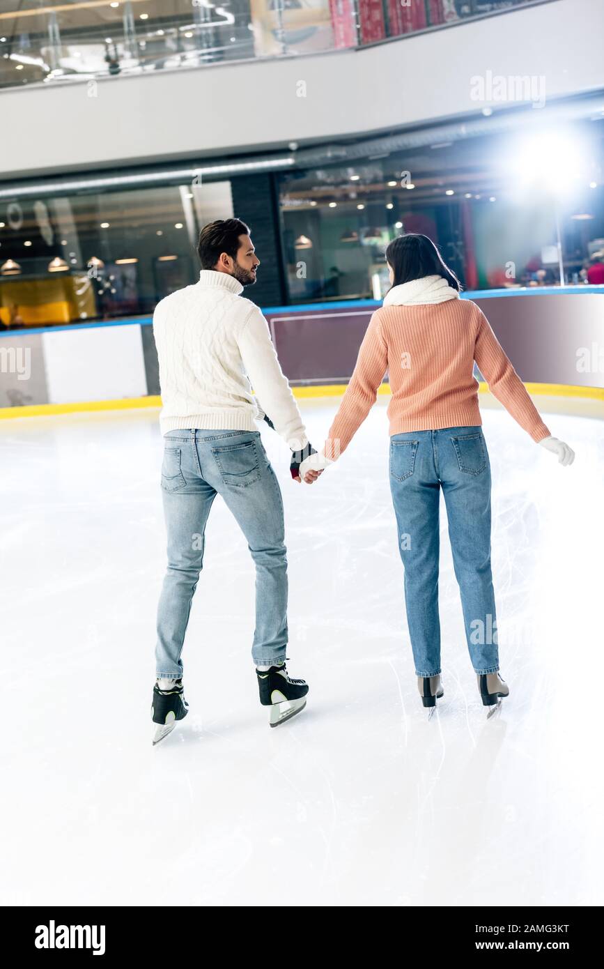 rear view of young couple holding hands and skating on rink Stock Photo ...