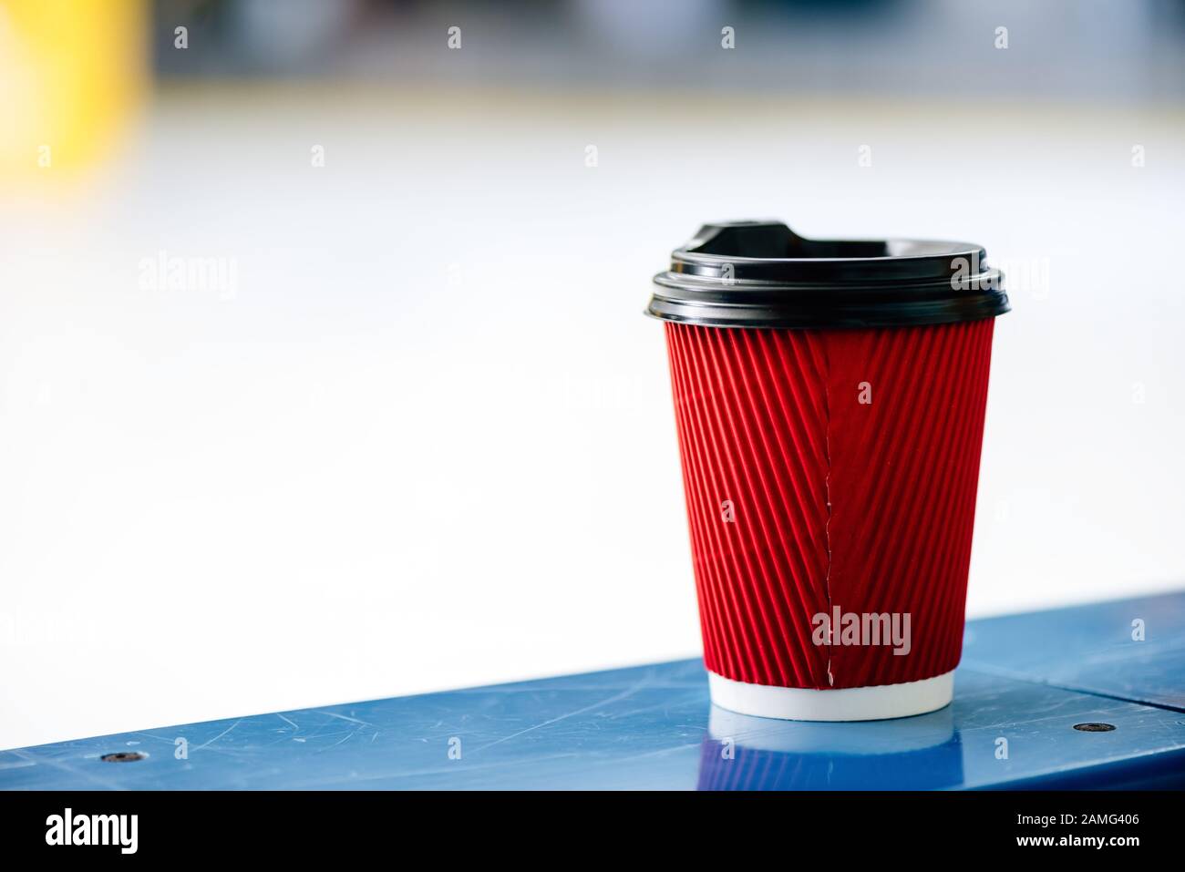 red disposable cup of coffee to go standing on railing of skating rink ...