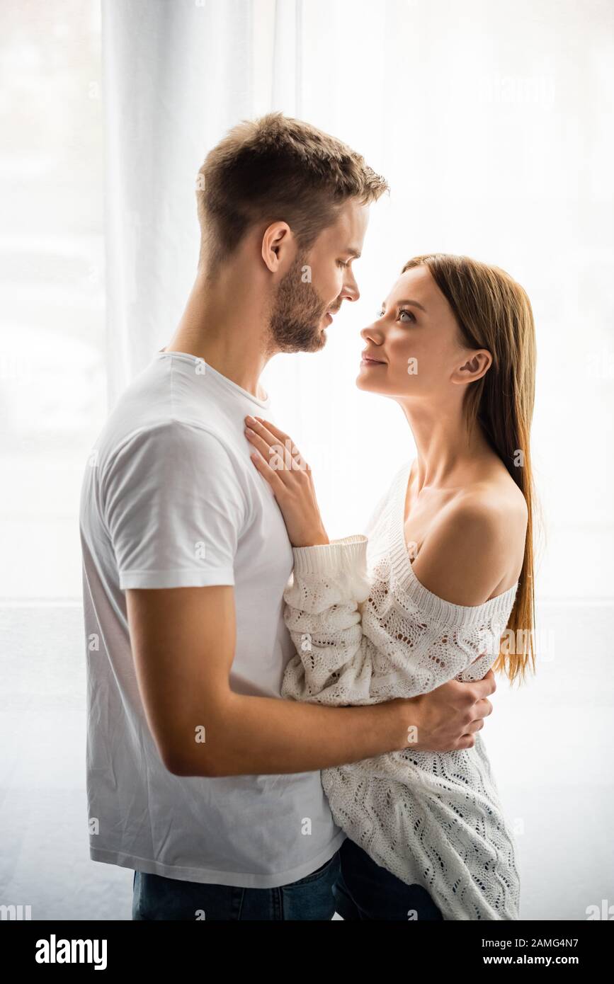 side view of handsome man hugging attractive and smiling woman in ...