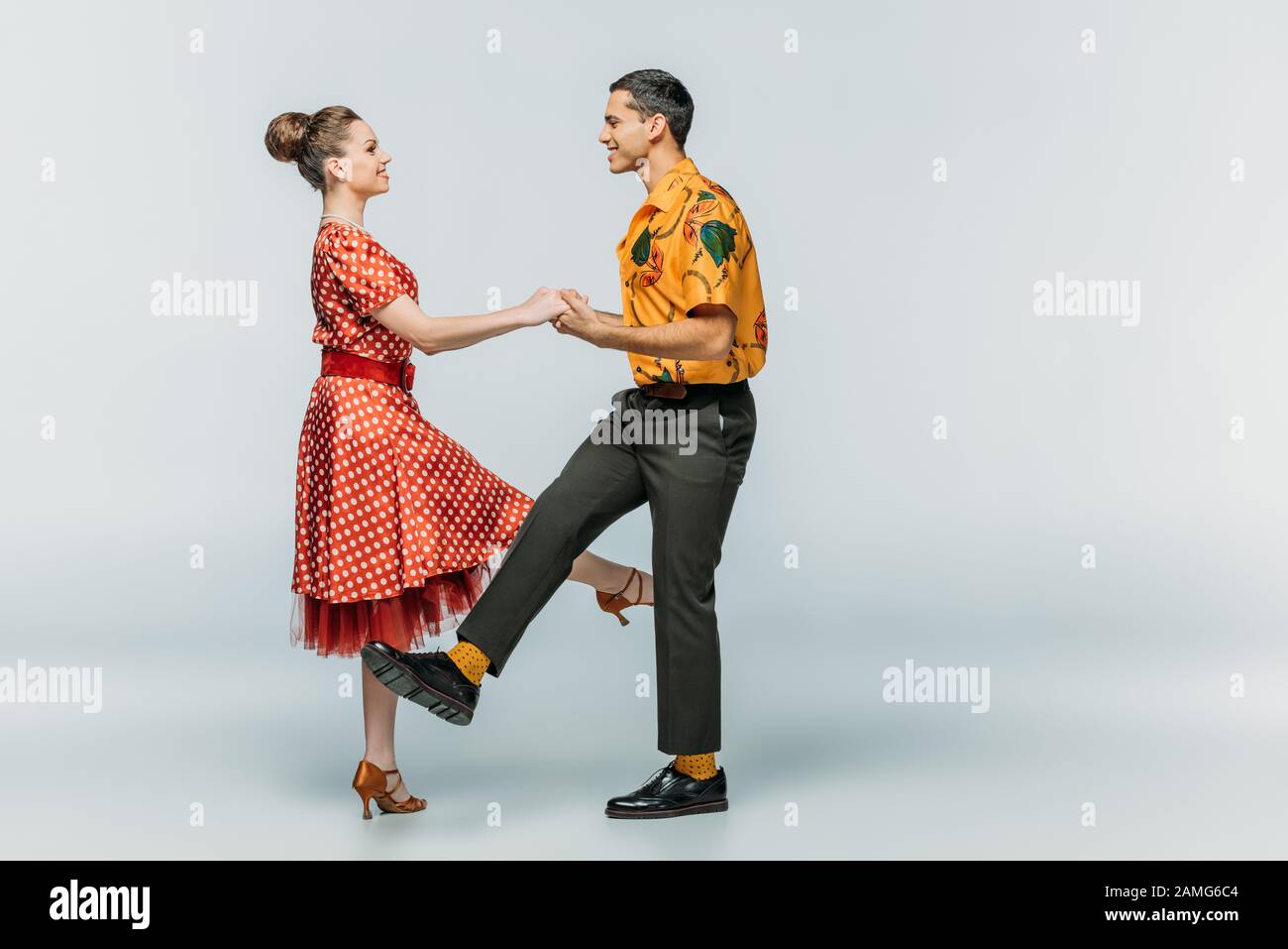 side view of smiling couple holding hands while dancing boogie-woogie ...