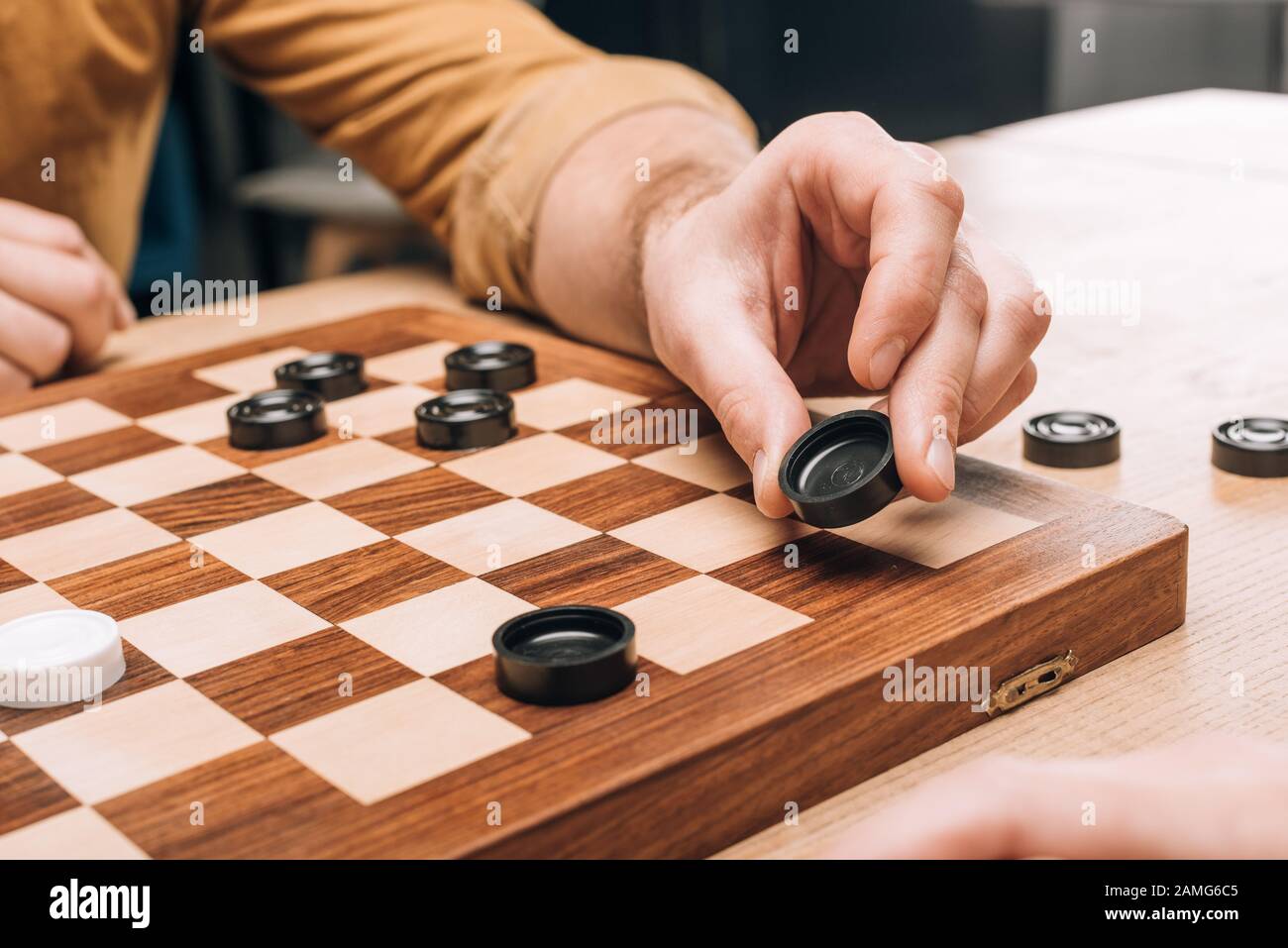 Selective focus of man holding black checker on wooden checkerboard ...