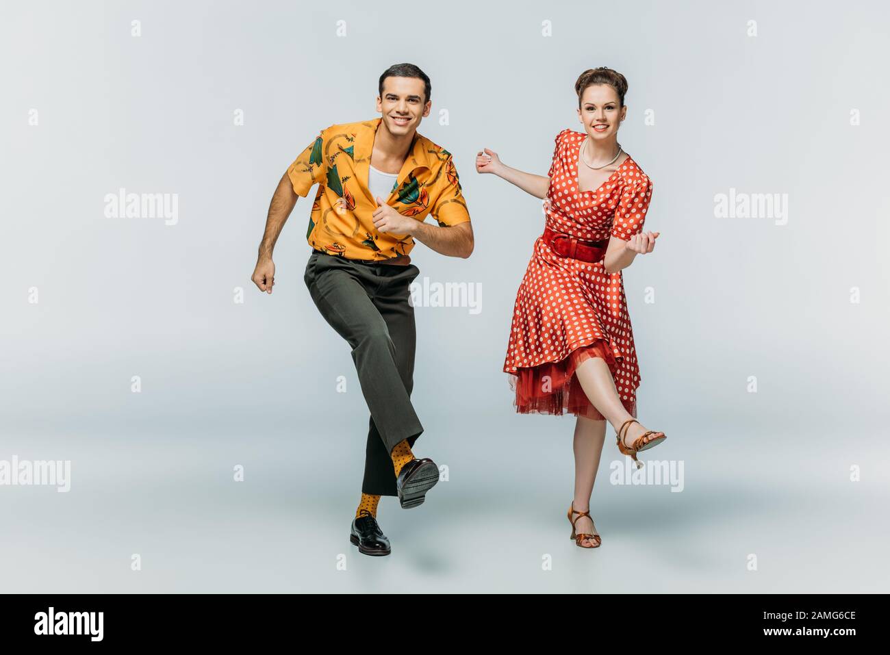 stylish couple looking at camera while dancing boogie-woogie on grey ...