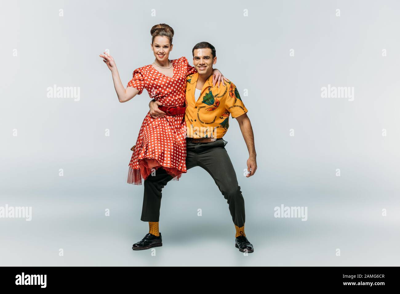 handsome dancer holding partner while dancing boogie-woogie on grey ...