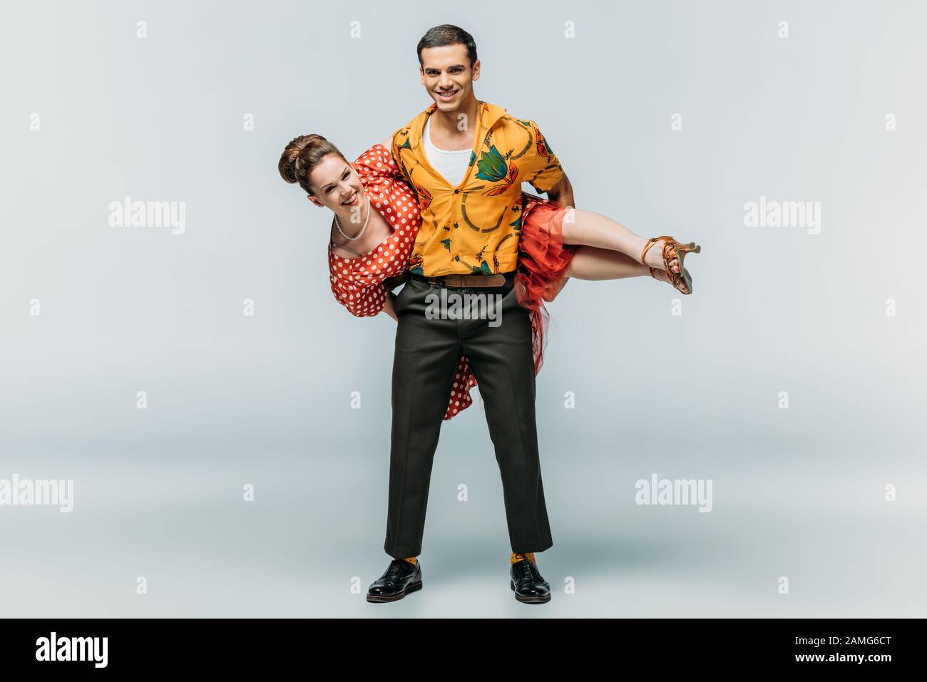 cheerful man holding woman while dancing boogie-woogie on grey ...