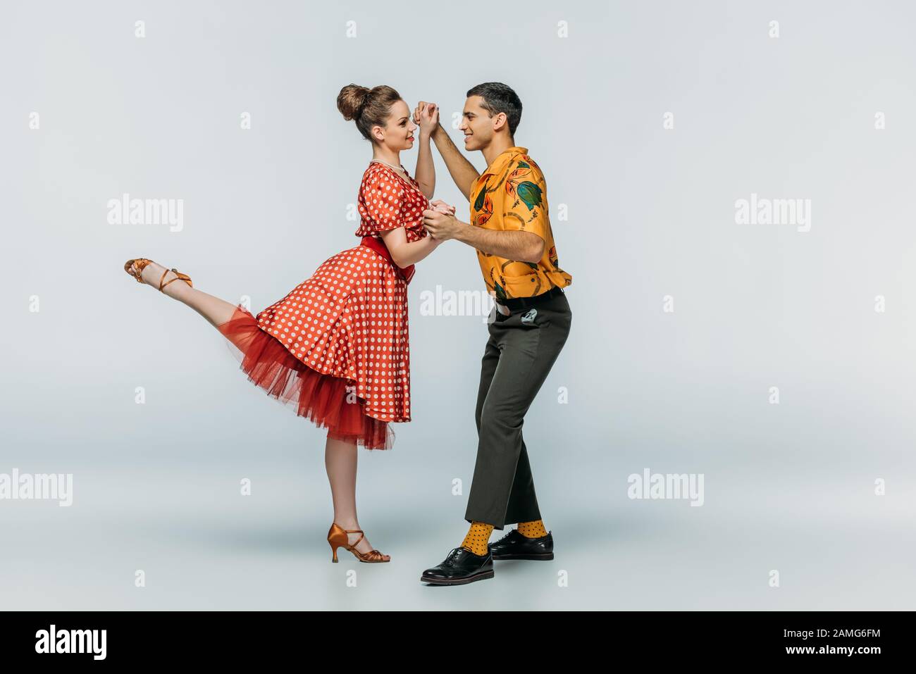 cheerful dancers holding hands while dancing boogie-woogie on grey ...