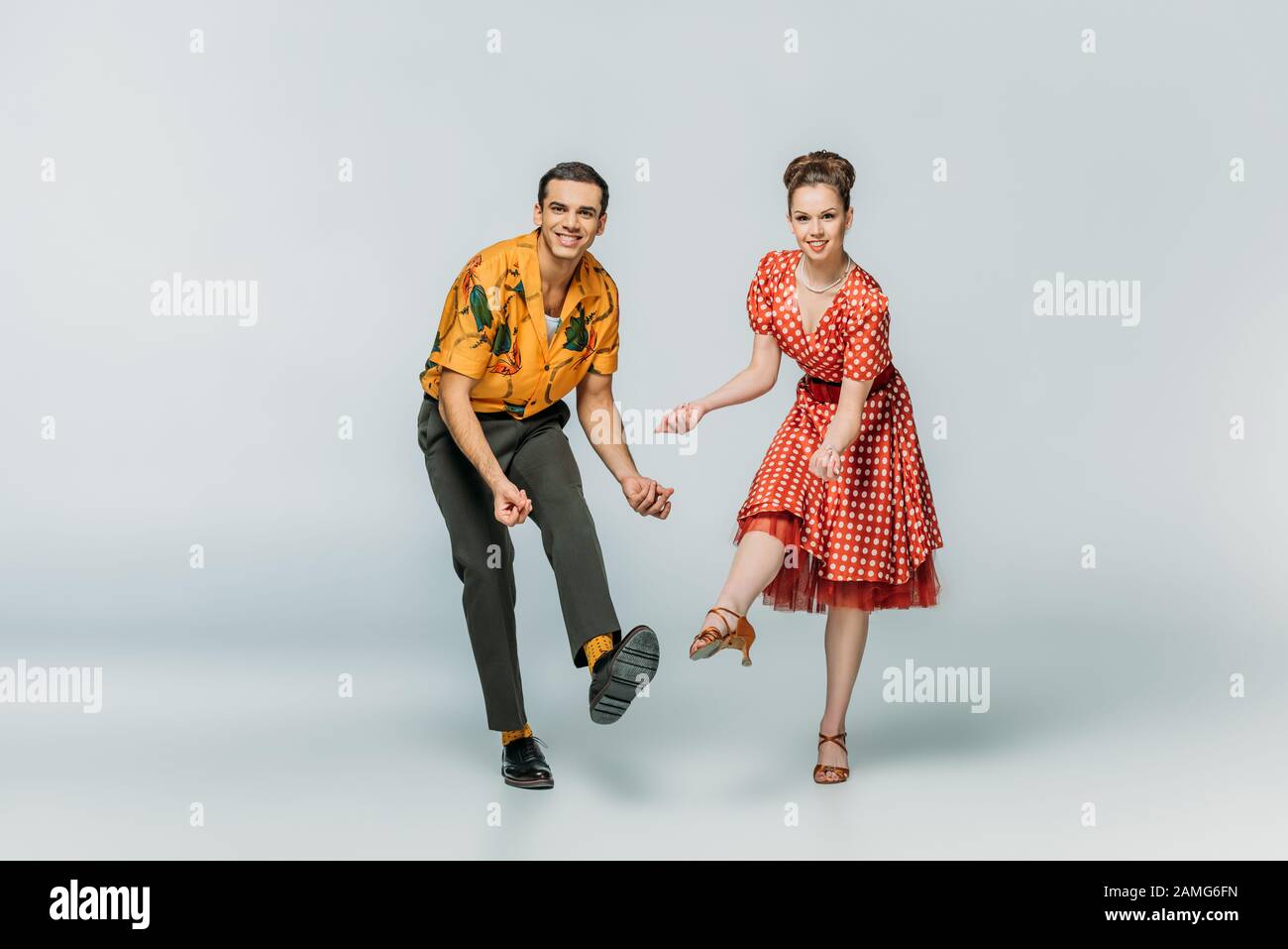 cheerful dancers looking at camera while dancing boogie-woogie on grey ...