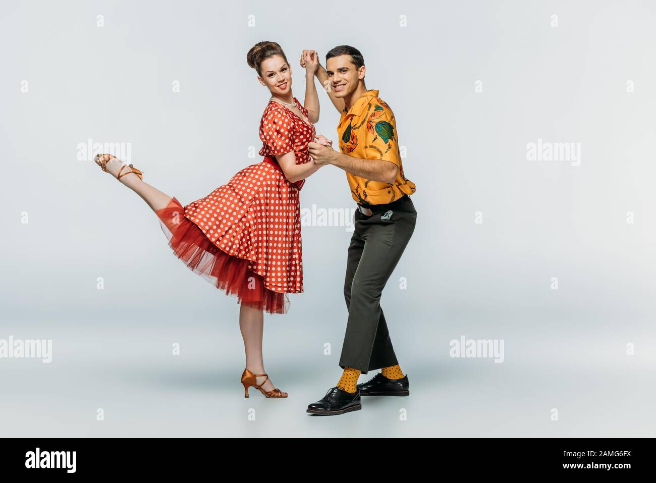 smiling dancers holding hands while dancing boogie-woogie on grey ...