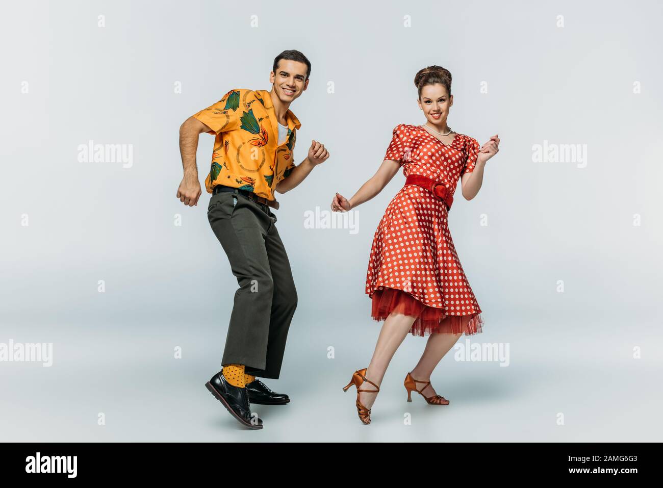 cheerful dancers looking at camera while dancing boogie-woogie on grey ...