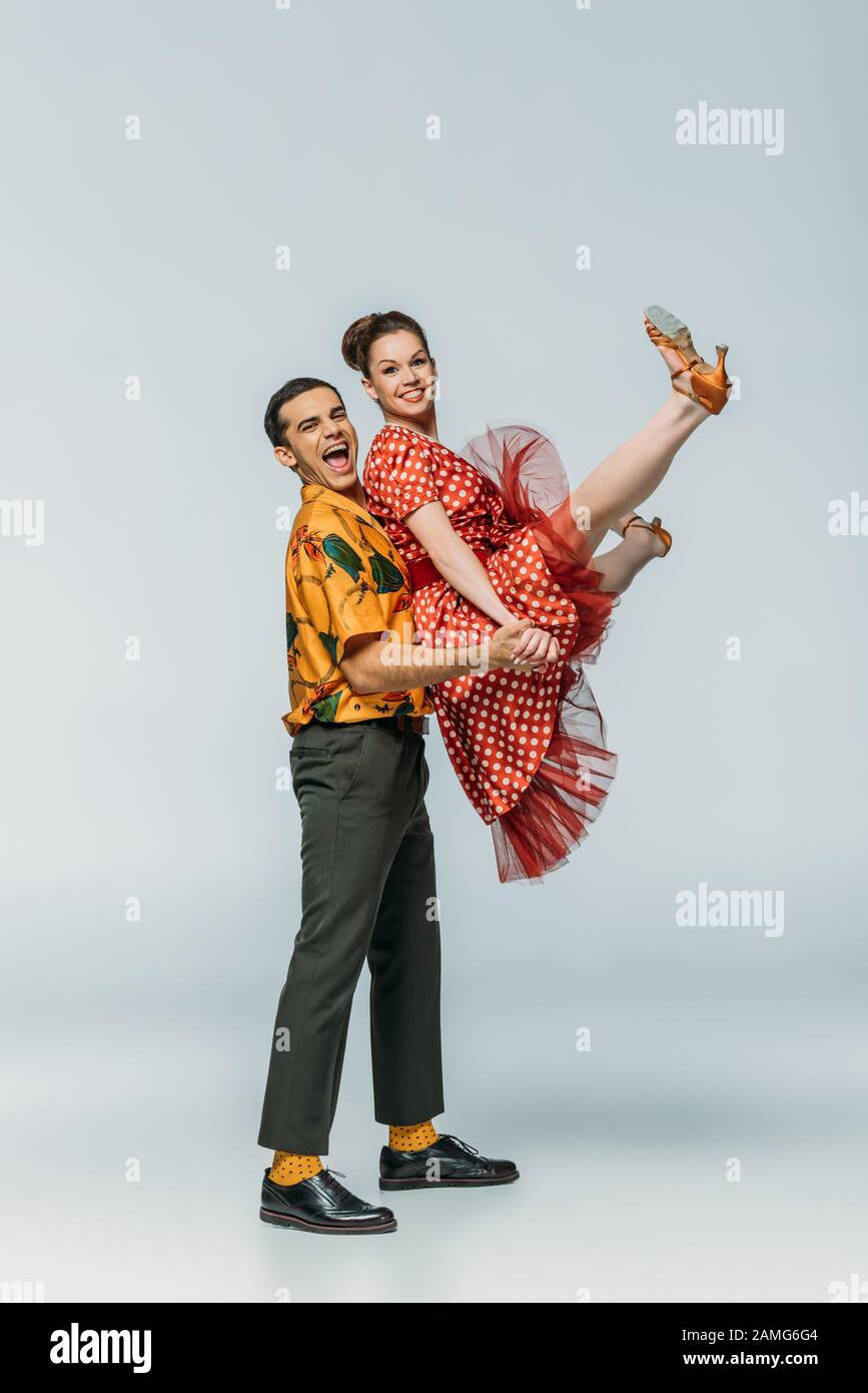 cheerful dancer holding partner while dancing boogie-woogie on grey ...