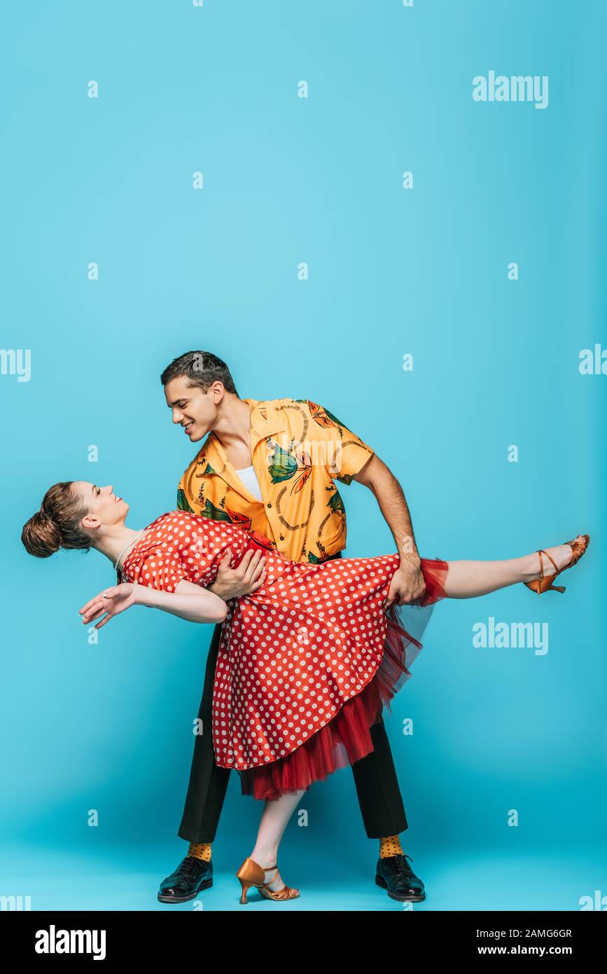 handsome dancer supporting partner while dancing boogie-woogie on blue ...