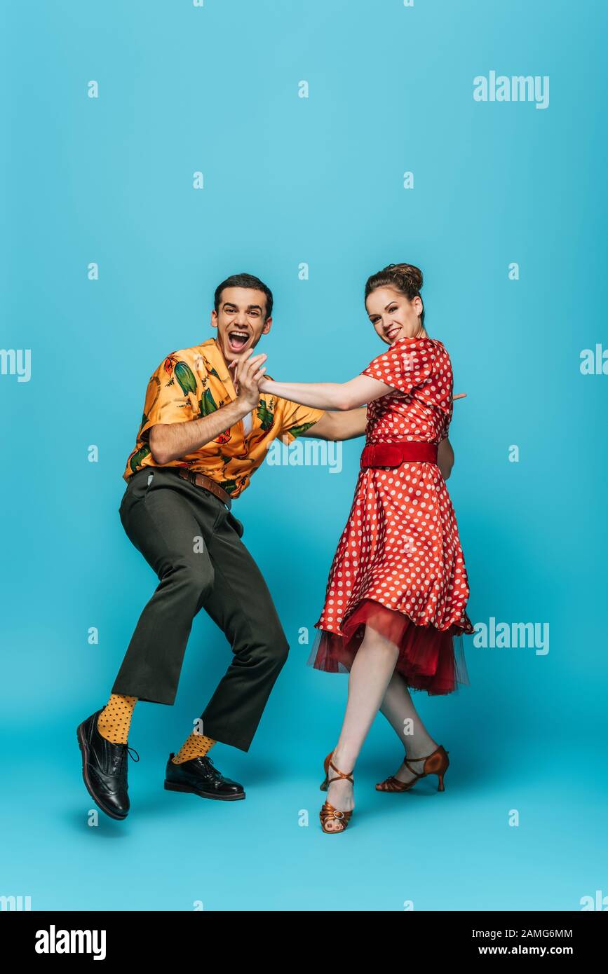 cheerful dancers holding hands while dancing boogie-woogie on blue ...