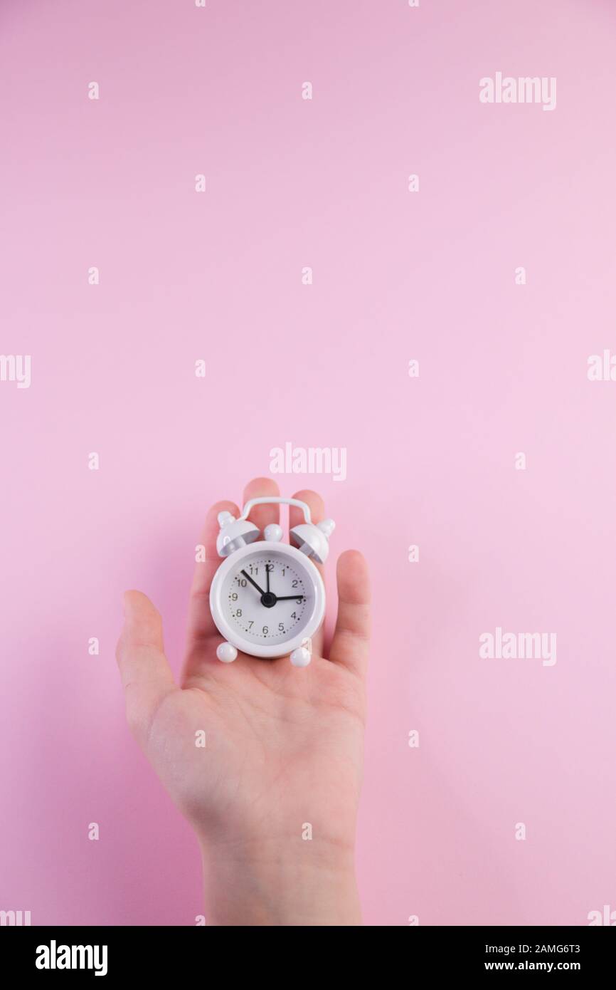 Pastel background with white alarm clock on pink background in hands ...