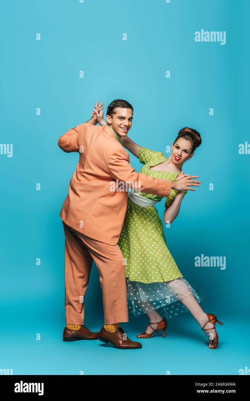 cheerful dancers looking at camera while dancing boogie-woogie on blue ...