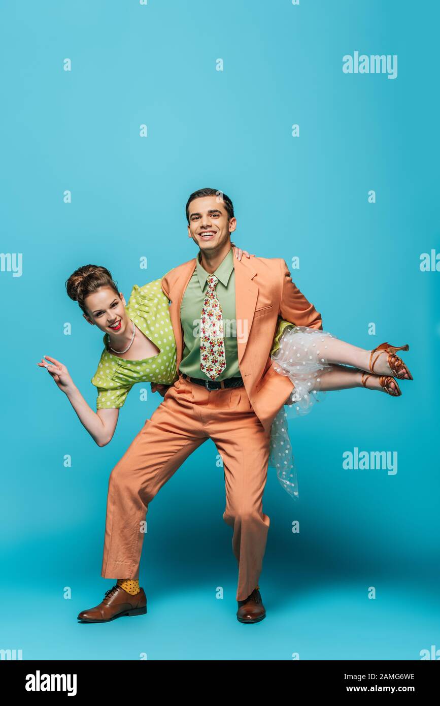 cheerful dancer holding girl while dancing boogie-woogie on blue ...