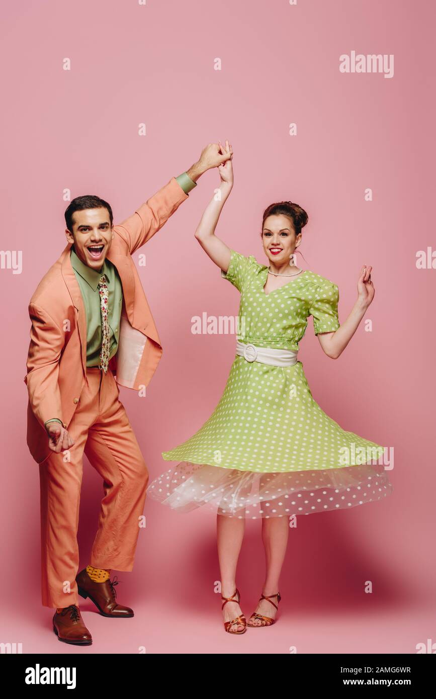 cheerful dancers holding hands while dancing boogie-woogie on pink ...
