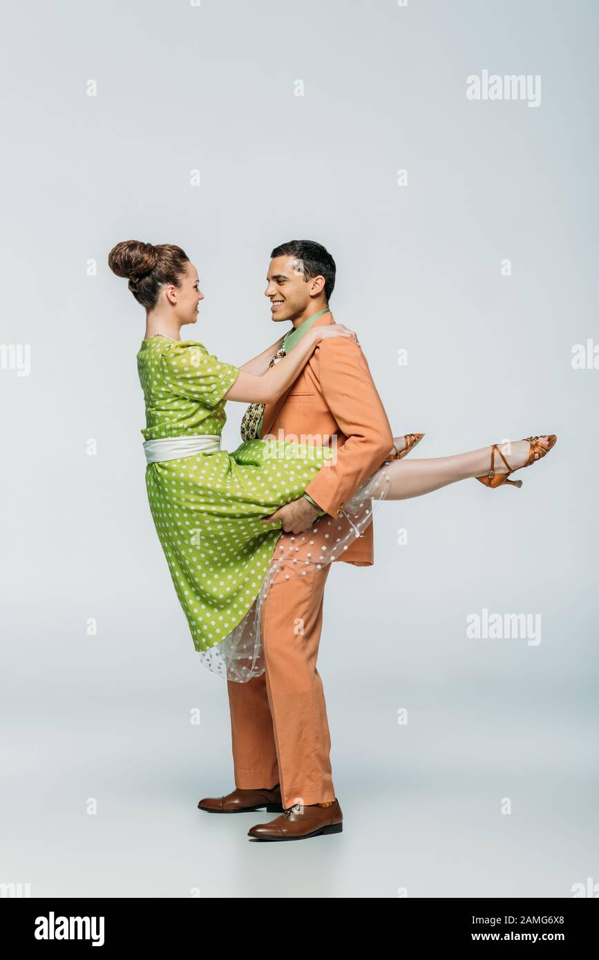 handsome dancer holding girl while dancing boogie-woogie on grey ...