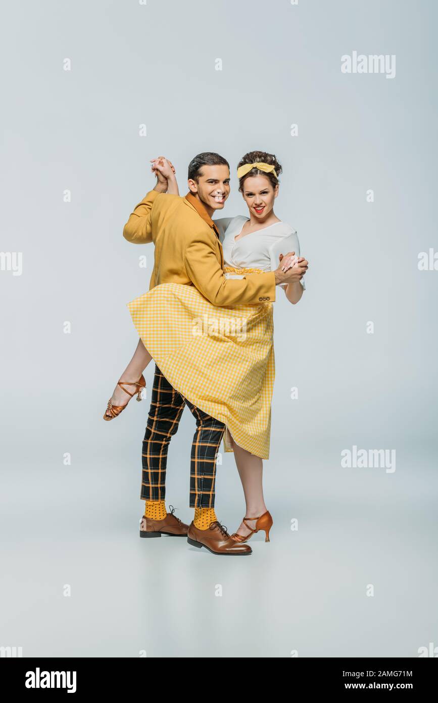 smiling dancers holding hands while dancing boogie-woogie on grey ...