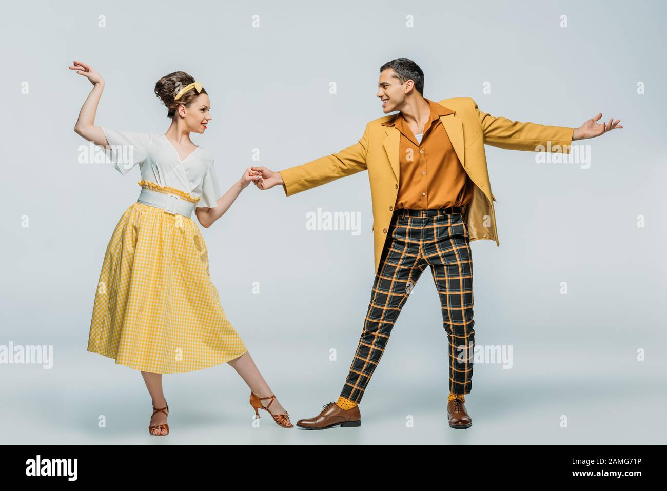 stylish dancers holding hands while dancing boogie-woogie on grey ...