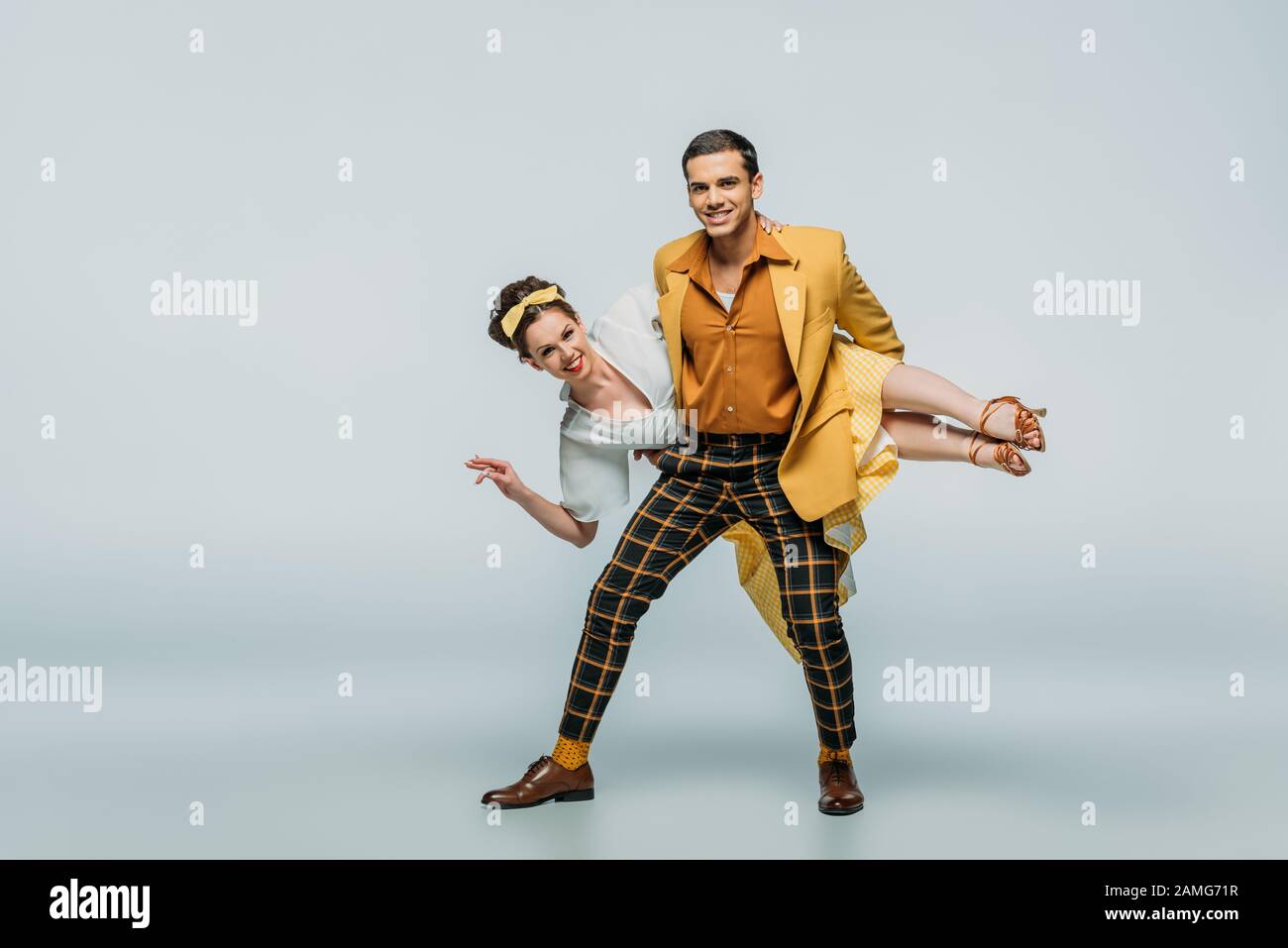 handsome dancer holding girl while dancing boogie-woogie on grey ...