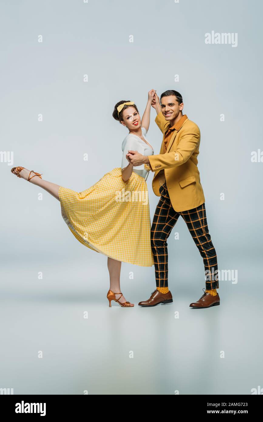 stylish dancers holding hands while dancing boogie-woogie on grey ...