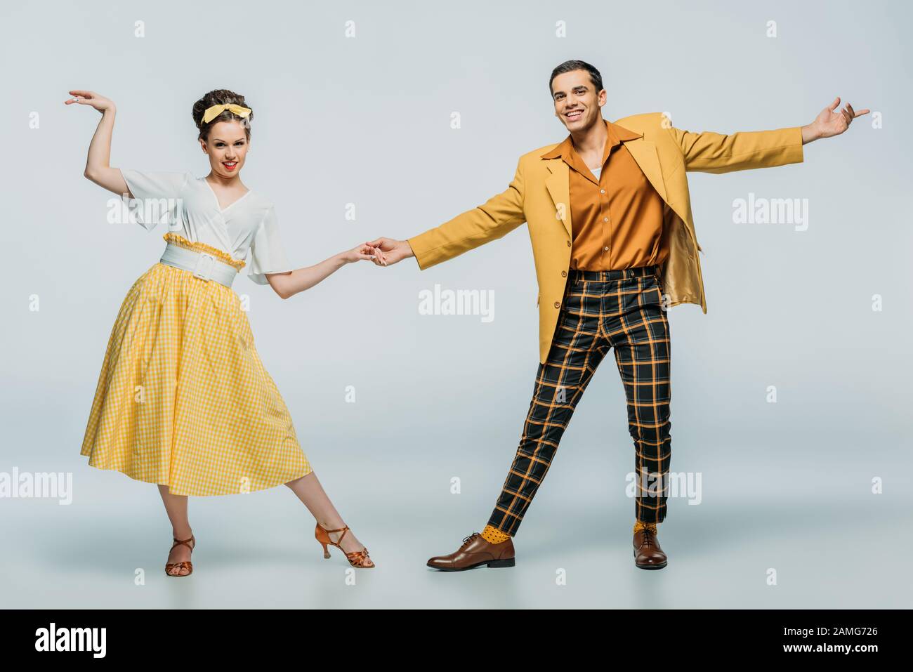 stylish dancers holding hands while dancing boogie-woogie on grey ...