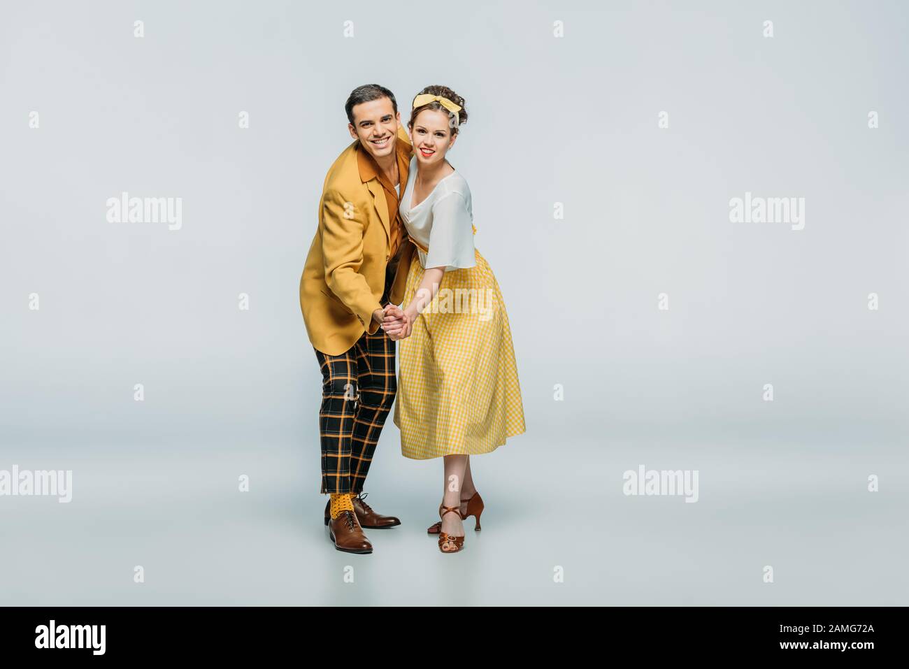 stylish dancers holding hands while dancing boogie-woogie on grey ...