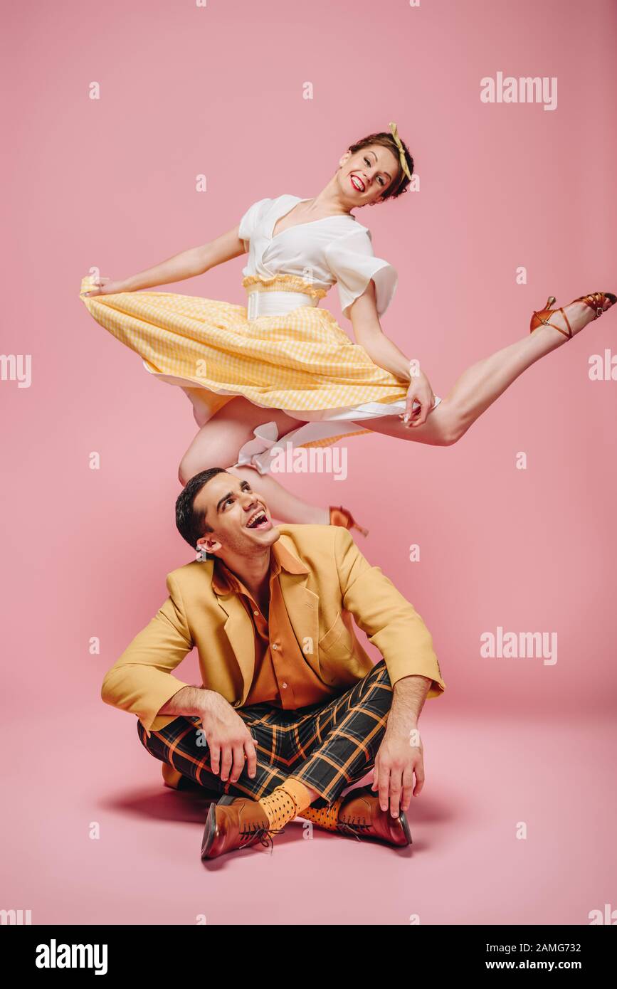cheerful man sitting on floor and happy girl jumping while dancing ...