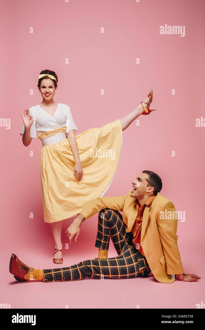 cheerful man sitting on floor and girl waving at camera while dancing ...