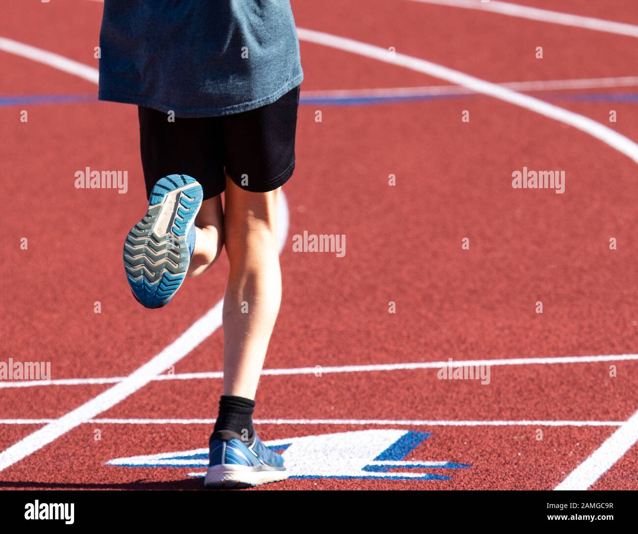 Rear view of a young male runner in lane four on a red track with white ...