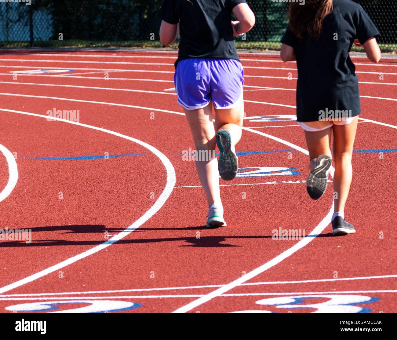 Rear view two high school teenagers running side by side on a track ...