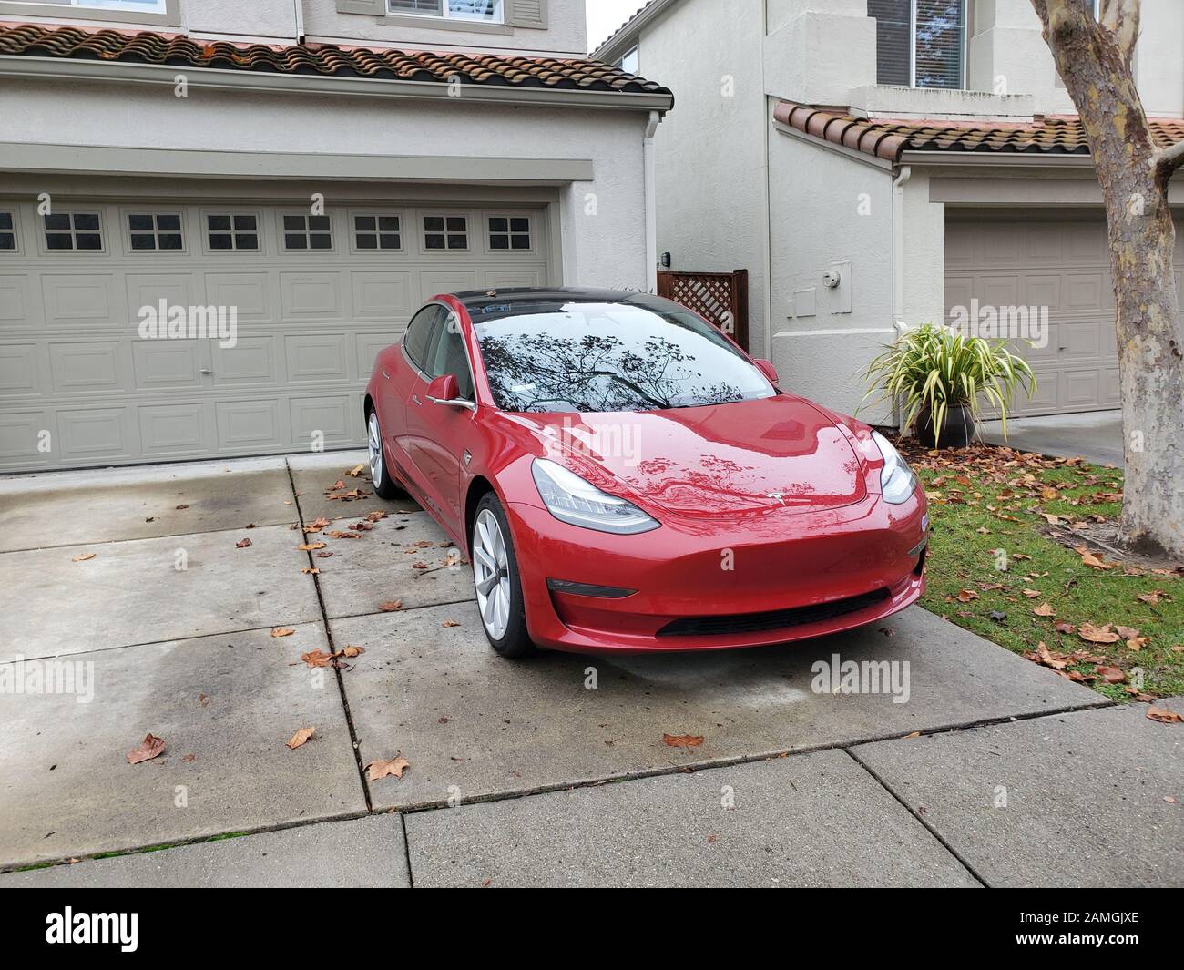 Red Tesla Model 3 automobile parked in the driveway of a suburban home ...
