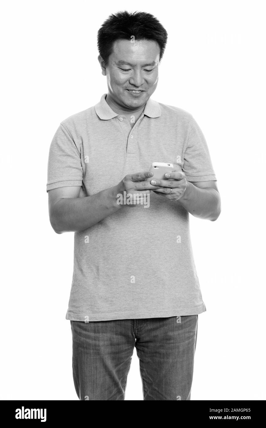 Studio shot of happy Japanese man smiling while using mobile phone ...