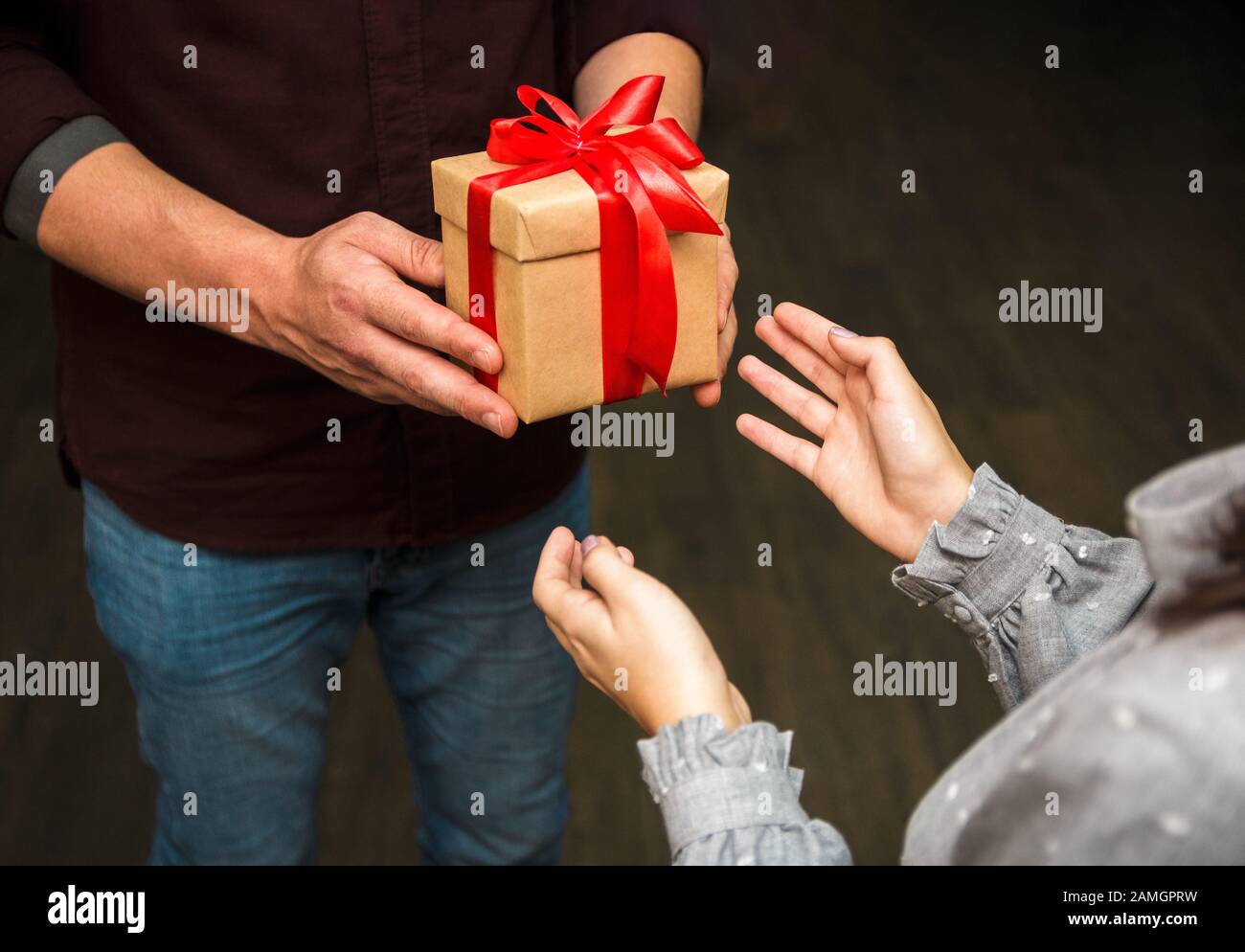 Close up view of hands of a man handing a gift package with a bow to a ...