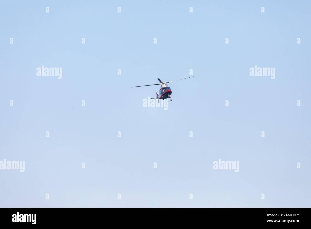 Front view of small red private helicopter against a blue sky with ...