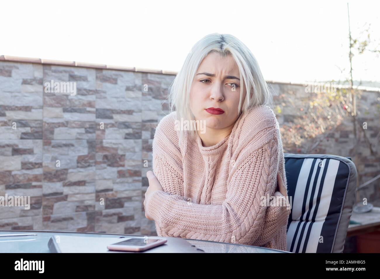 Sad woman sitting on a chair in a terrace arms crossed Stock Photo - Alamy