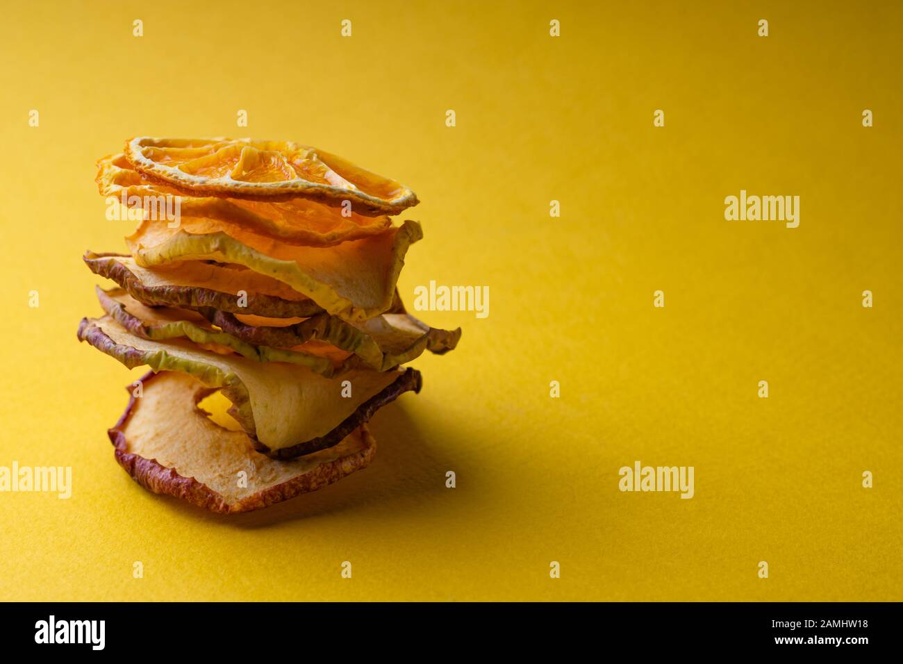 Pyramid of chips of dried apples and orange on a yellow background and ...