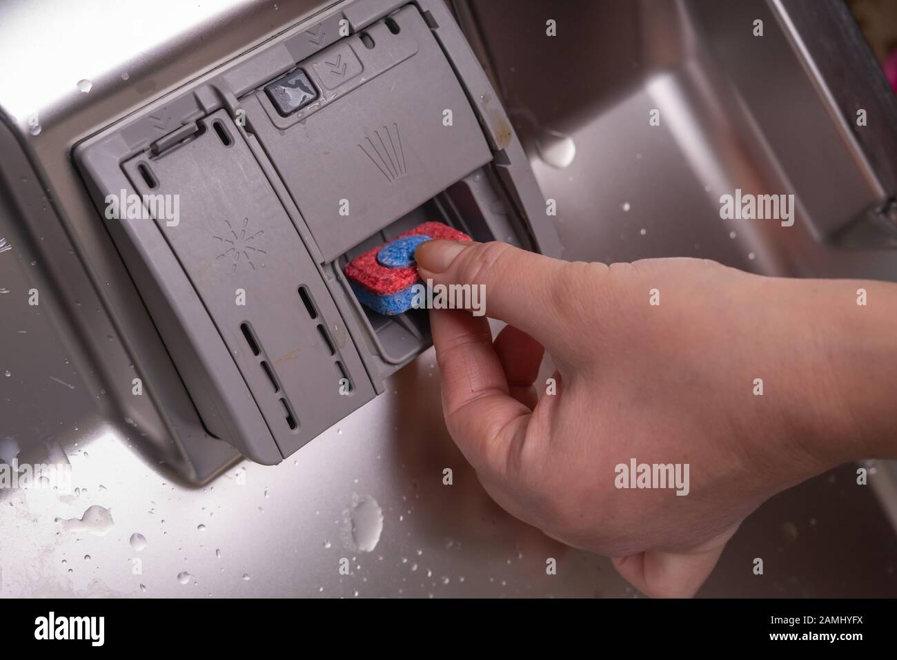 Installing detergent in the dishwasher. A female hand inserts a blue ...