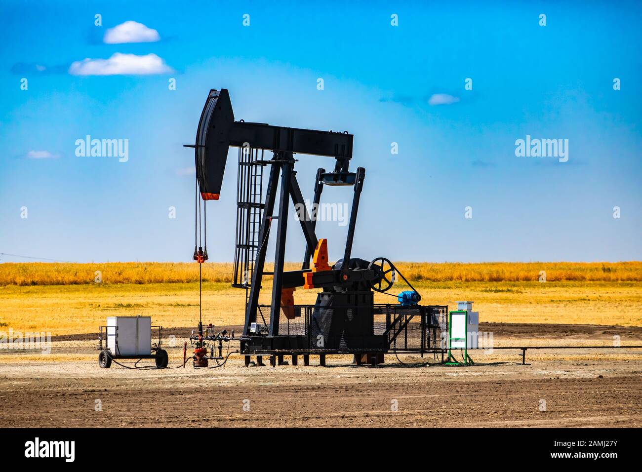 A modern black pumpjack over an oil well is seen in a golden field ...