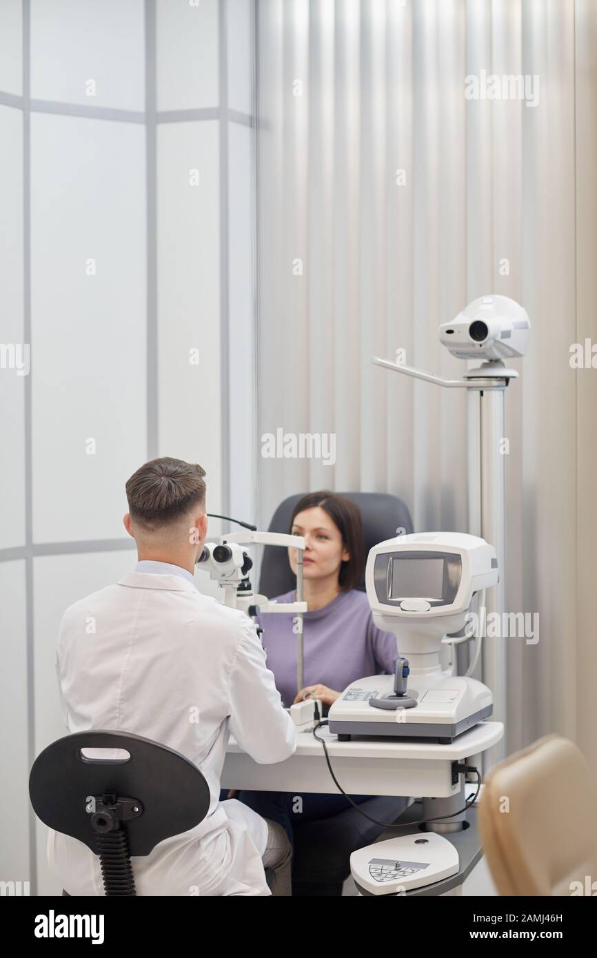 Vertical portrait of young woman using machines during vision test in ...