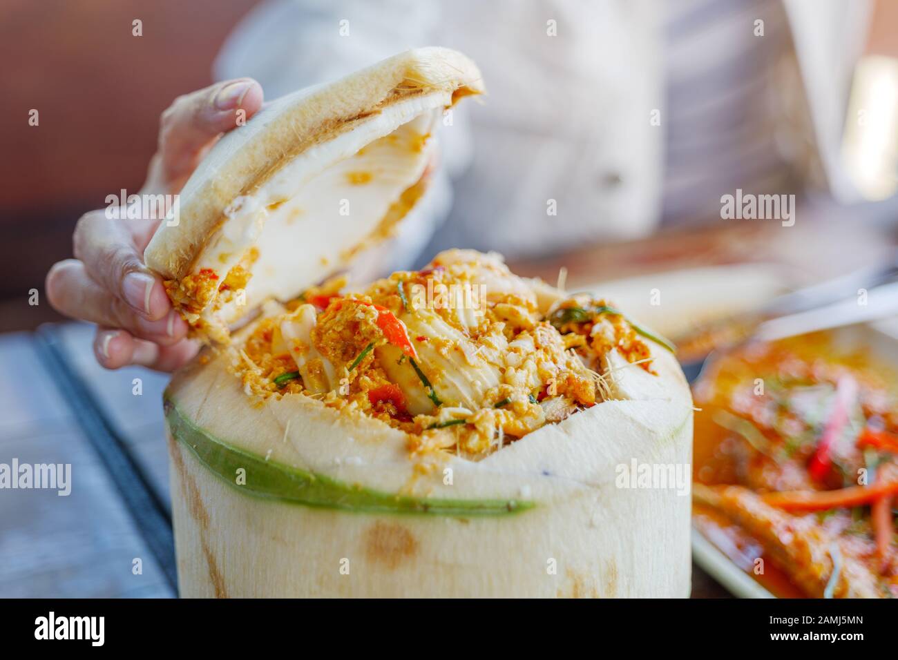 Hand open top of coconut with inner of Thai spicy steamed fish and ...