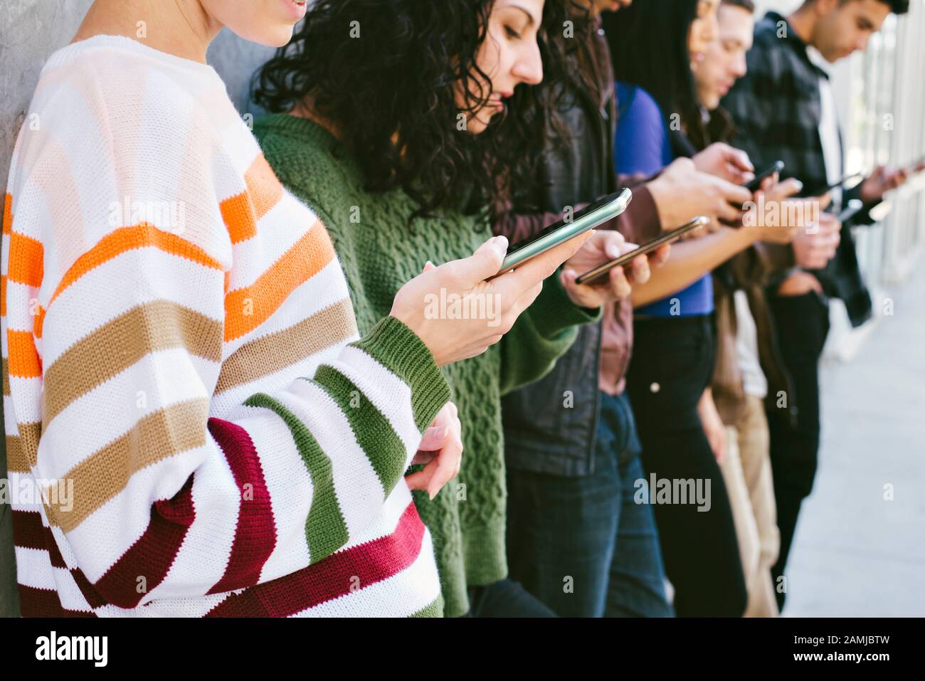 Young men and women look at their smart phones - Standing against a ...