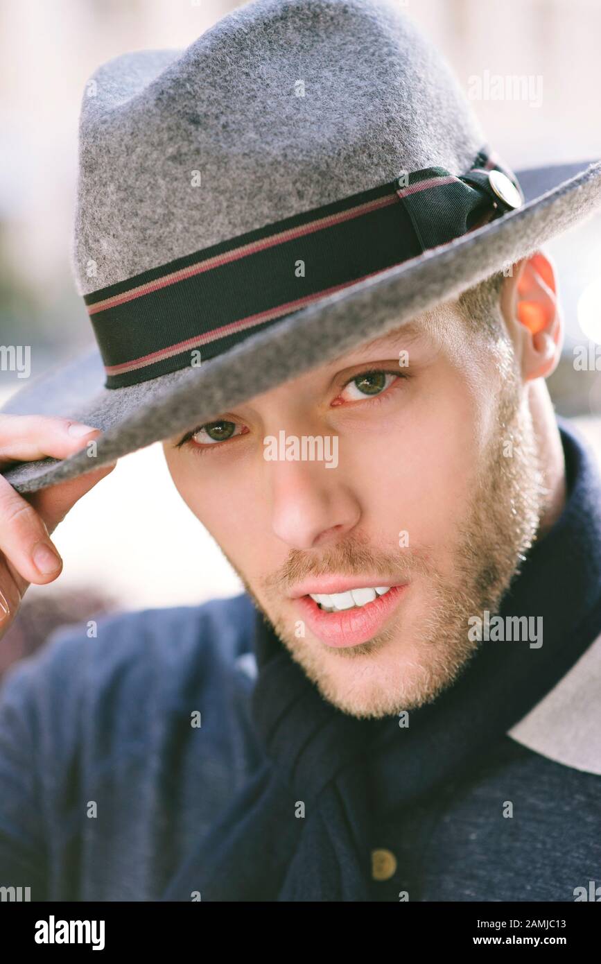 Millennial male looks at the camera while placing a hand on his hat ...