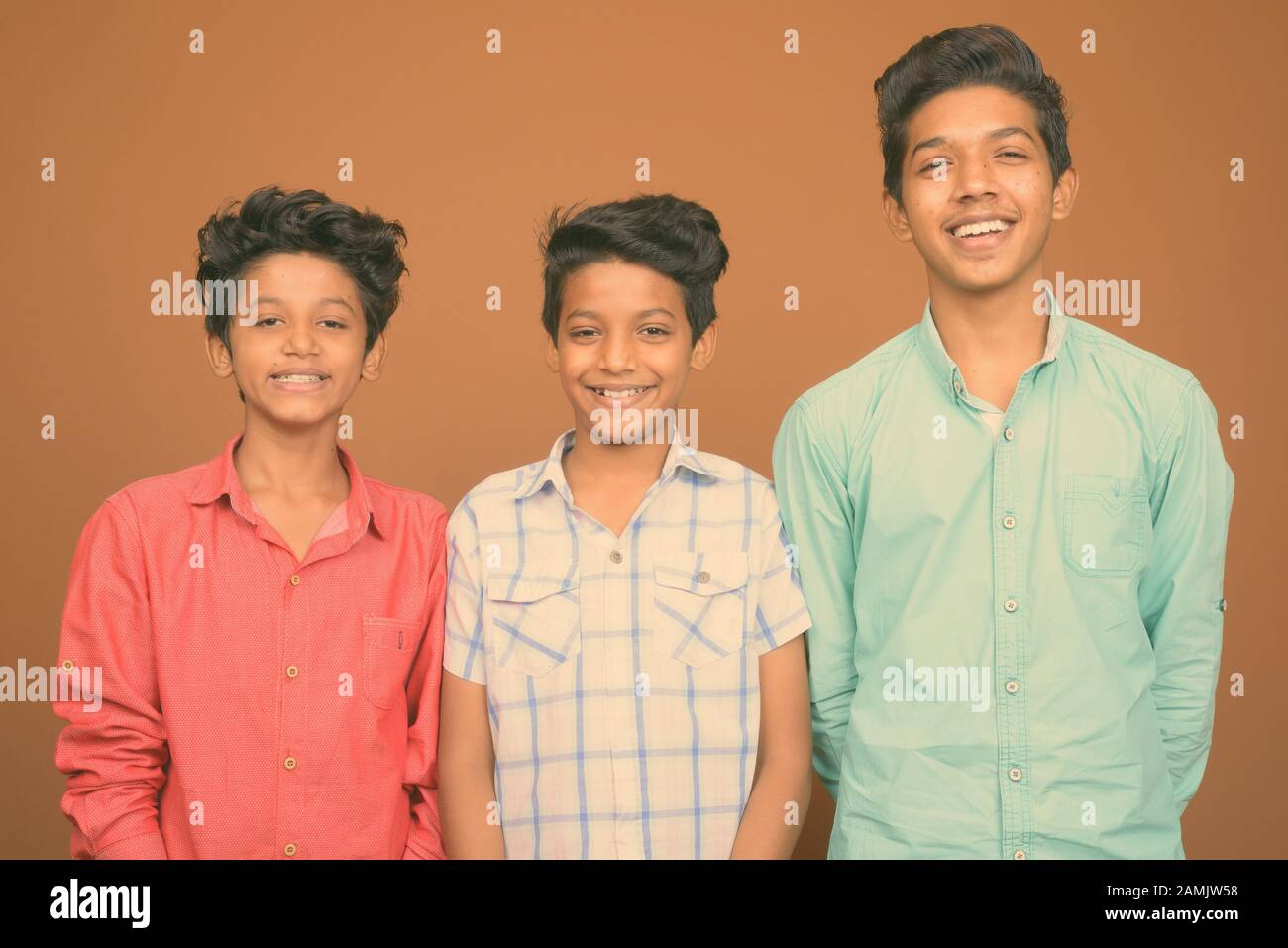 Studio shot of three young Indian brothers together against brown ...