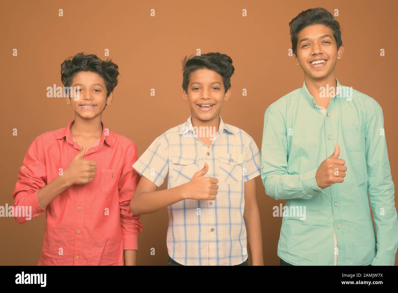 Studio shot of three young Indian brothers together against brown ...