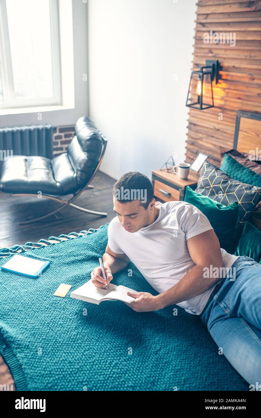 Guy writing with a pen in notebook lying on the bed Stock Photo - Alamy